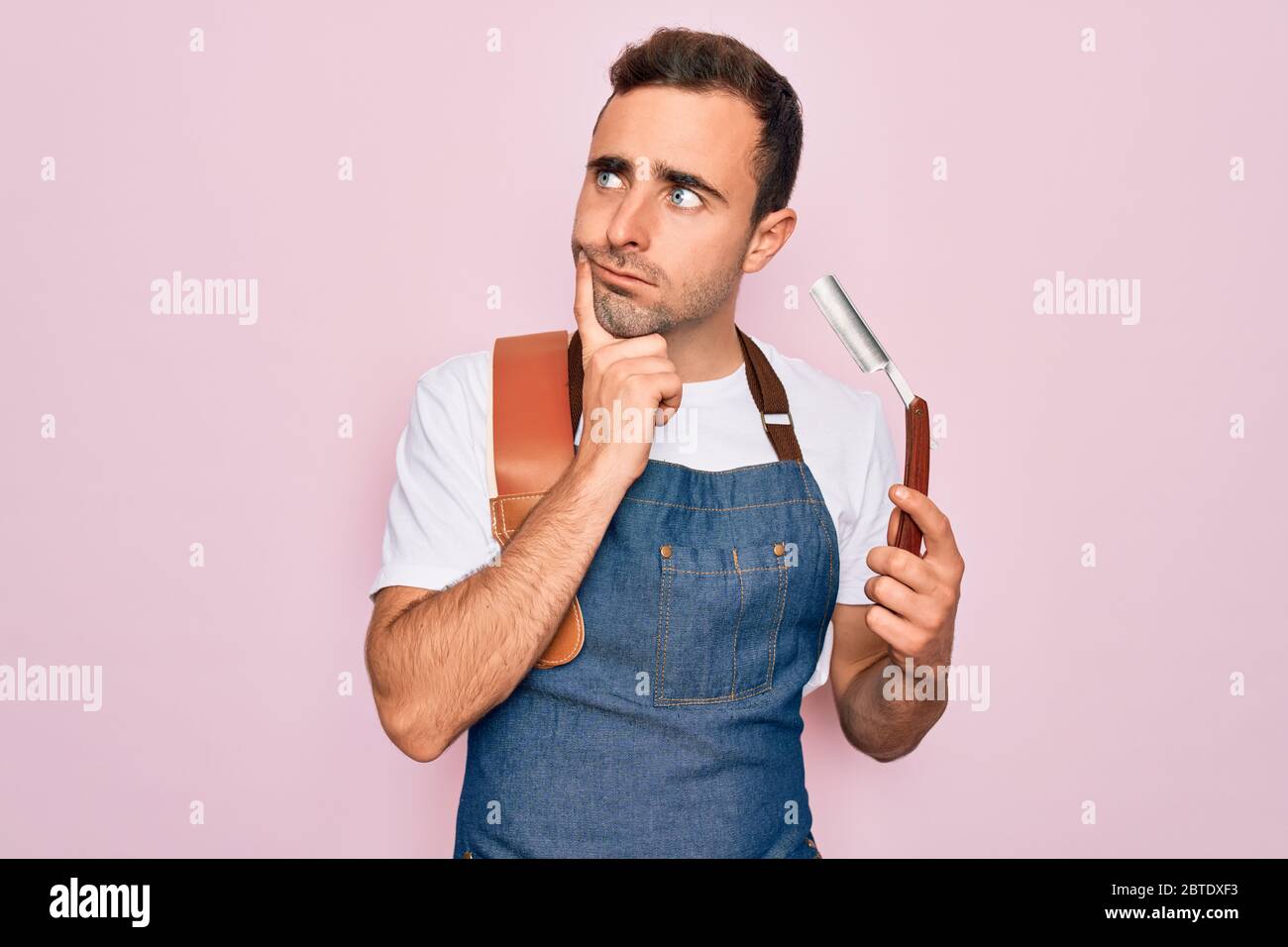 Handsome barber man with blue eyes wearing apron using razor blade over ...
