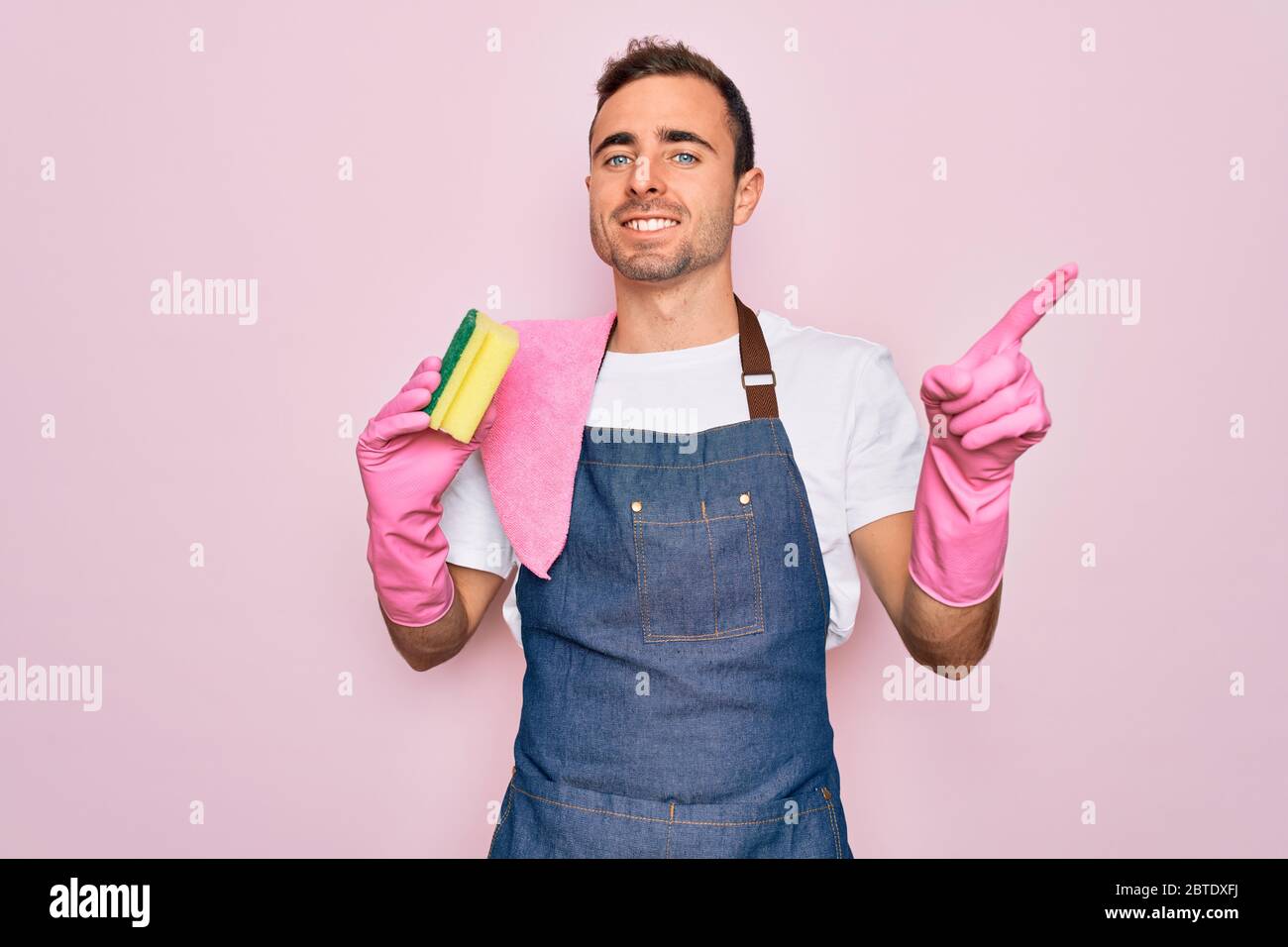 Young cleaner man with blue eyes cleaning wearing apron and gloves ...