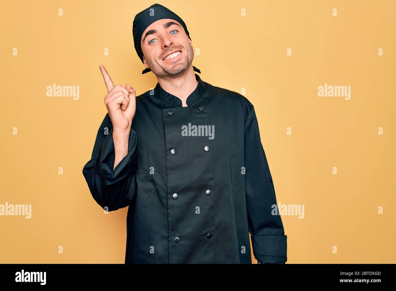 Young handsome cooker man with blue eyes wearing uniform and hat over ...