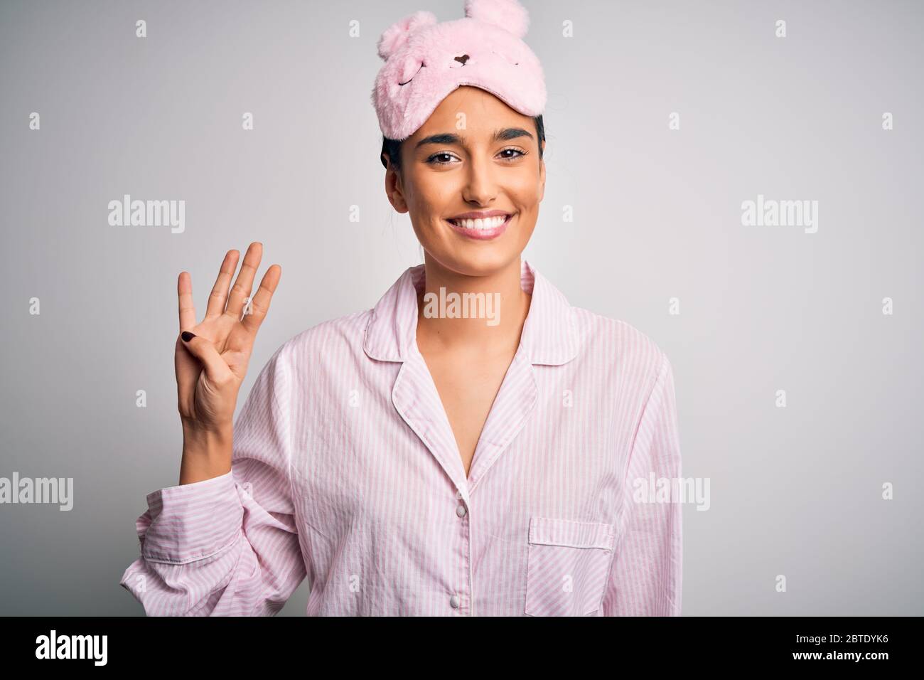 Young beautiful brunette woman wearing pajama and sleep mask over white ...