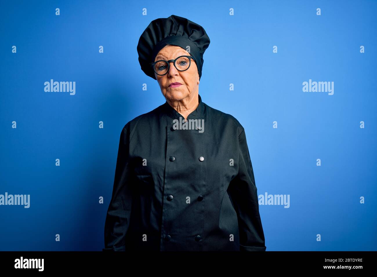 Senior beautiful grey-haired chef woman wearing cooker uniform and hat ...