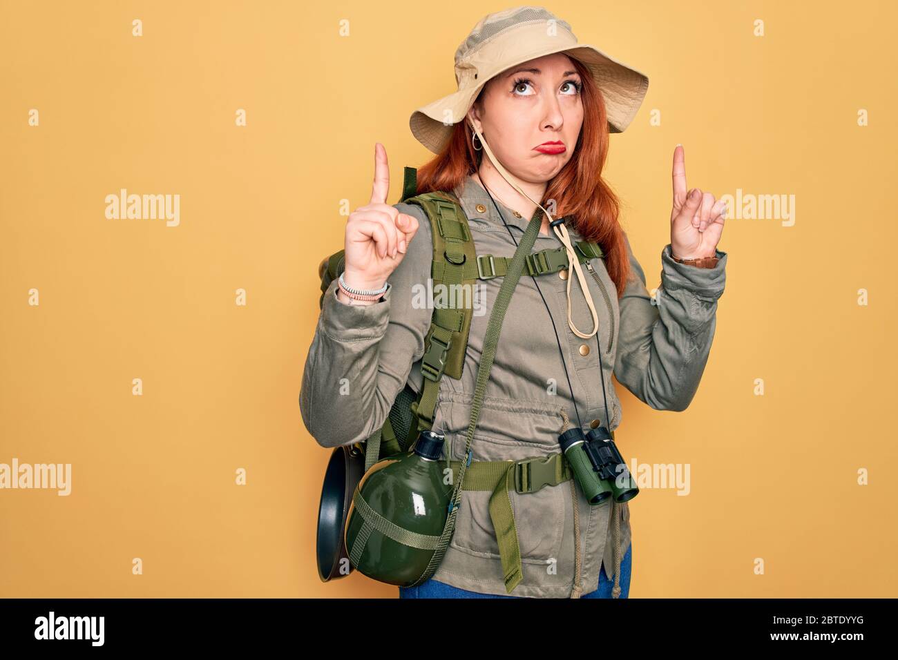 Young redhead backpacker woman hiking wearing backpack and hat over ...