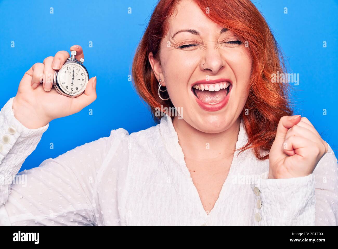 Young beautiful redhead woman doing countdown using stopwatch over blue ...
