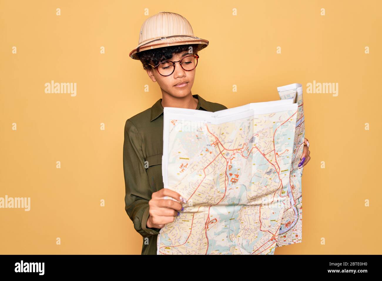 Beautiful african american explorer woman wearing hat holding city map ...