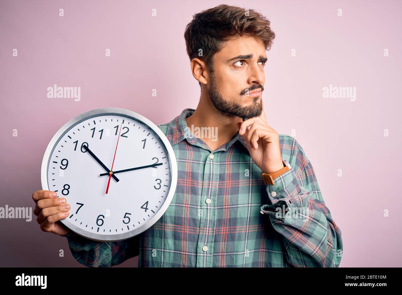 Young man with beard doing countdown using big clock over isolated pink ...