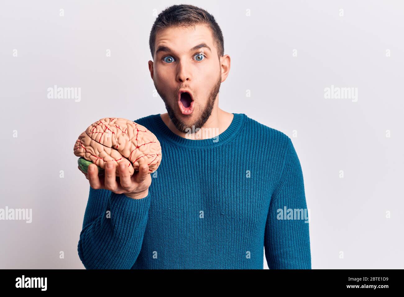 Young handsome man holding brain scared and amazed with open mouth for ...