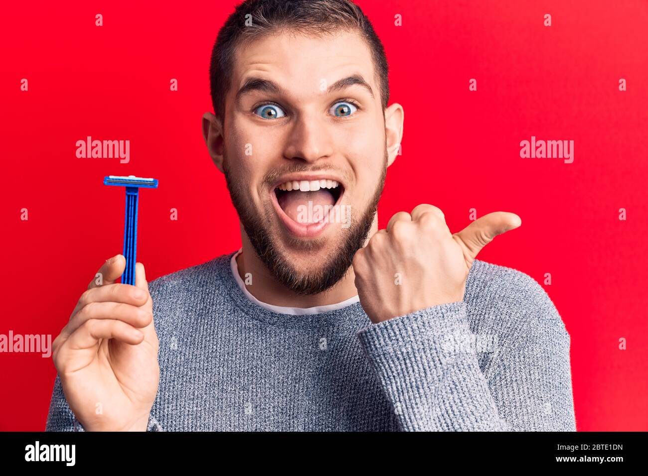 Young handsome man holding shave razor pointing thumb up to the side ...