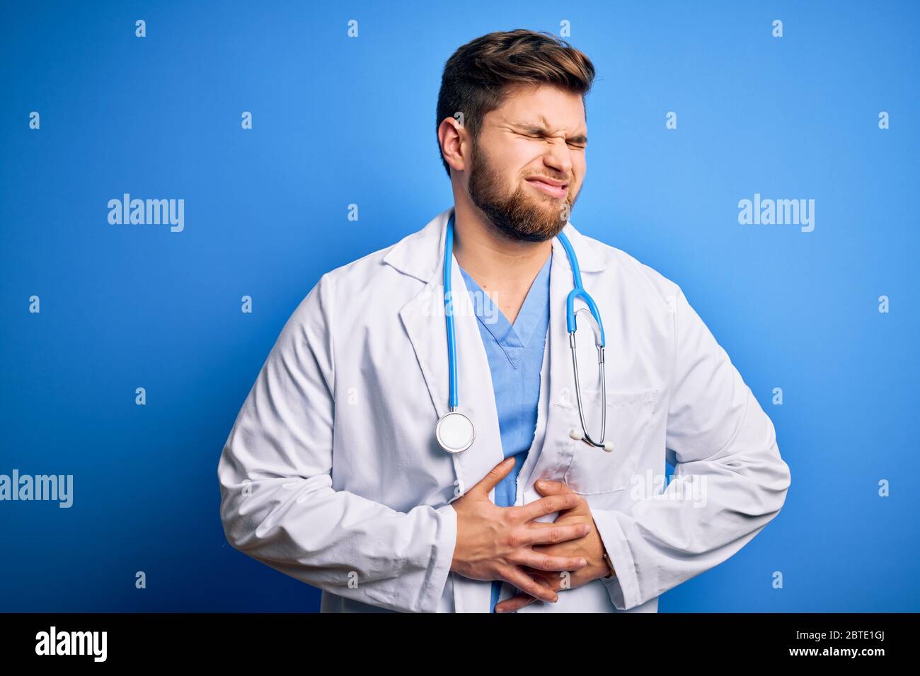Young blond doctor man with beard and blue eyes wearing white coat and ...