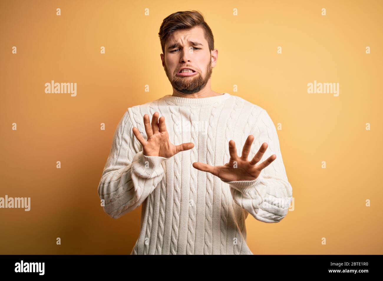 Young blond man with beard and blue eyes wearing white sweater over ...