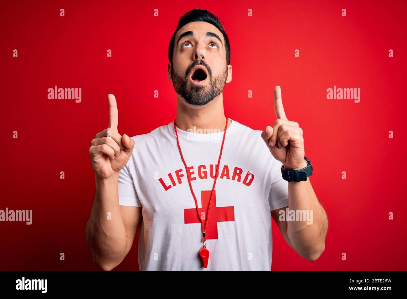 Young handsome lifeguard man with beard wearing whistle over isolated ...