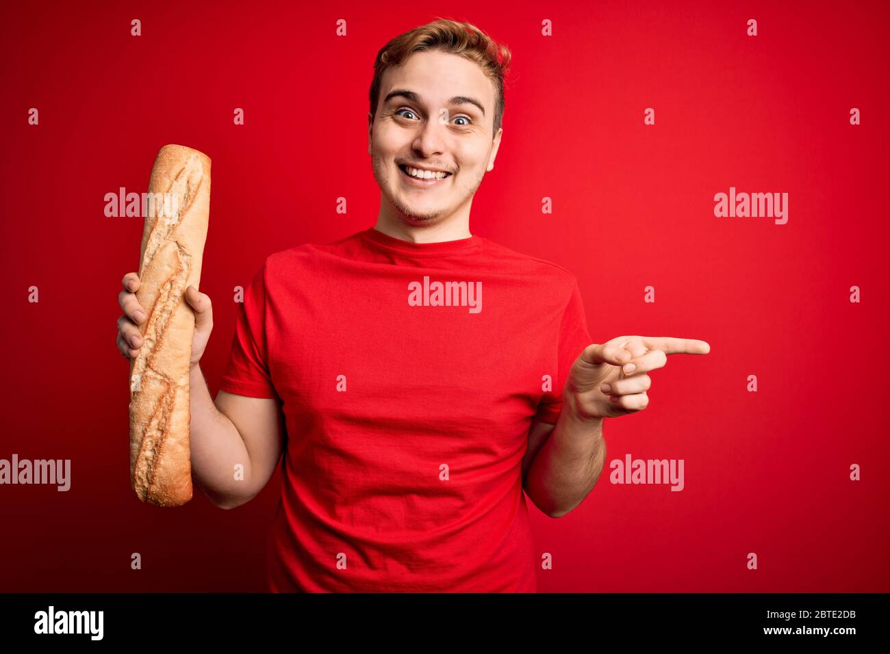 Young handsome redhead man holding fresh homemade bread over isolated ...