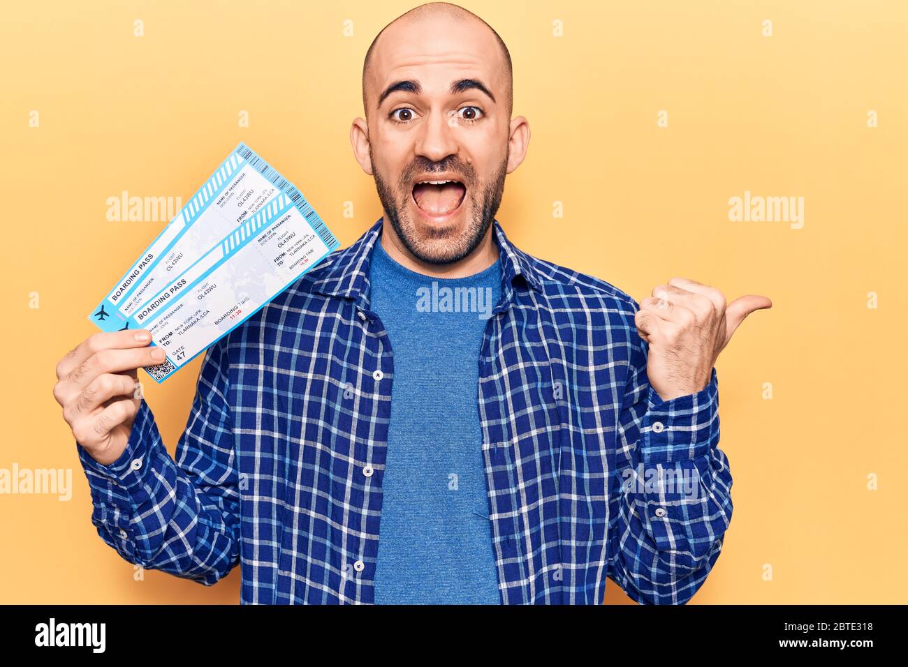 Young handsome bald man holding airline boarding pass pointing thumb up ...