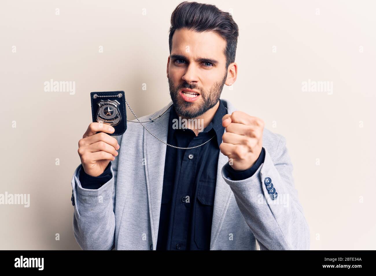 Young handsome man with beard holding police badge annoyed and ...
