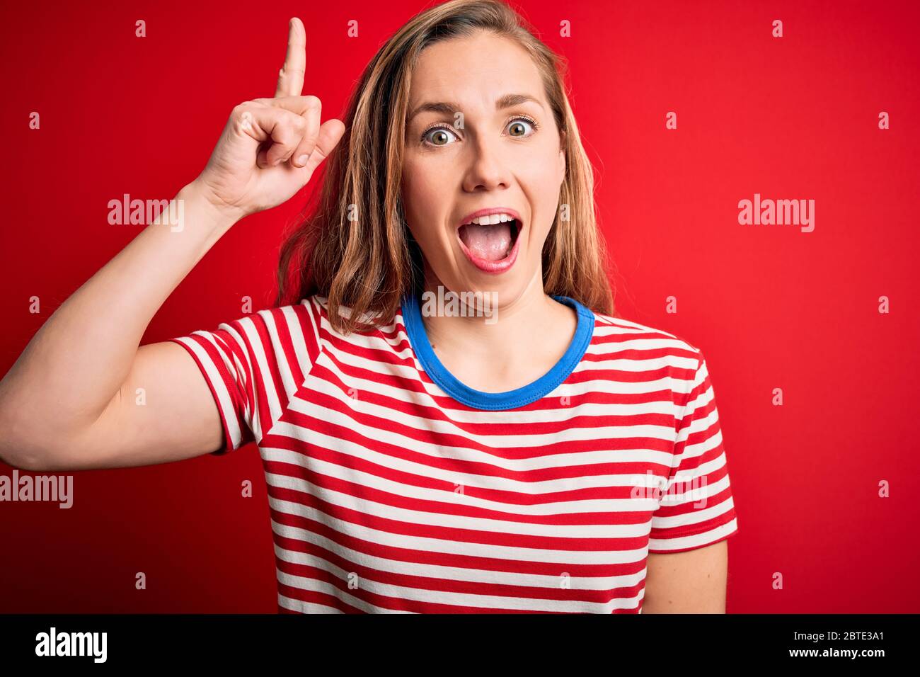 Young Beautiful Blonde Woman Wearing Casual Striped T Shirt Over Isolated Red Background