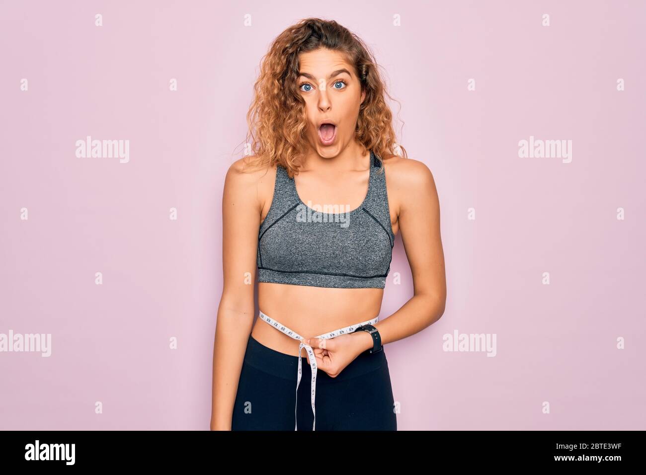 Young blonde sporty woman with blue eyes controlling weight using tape ...