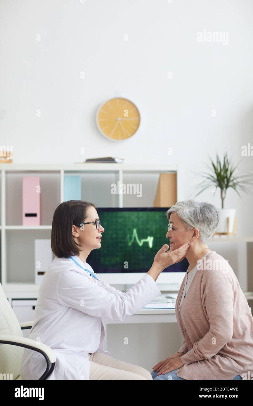 Vertical side view portrait of young female doctor examining senior ...