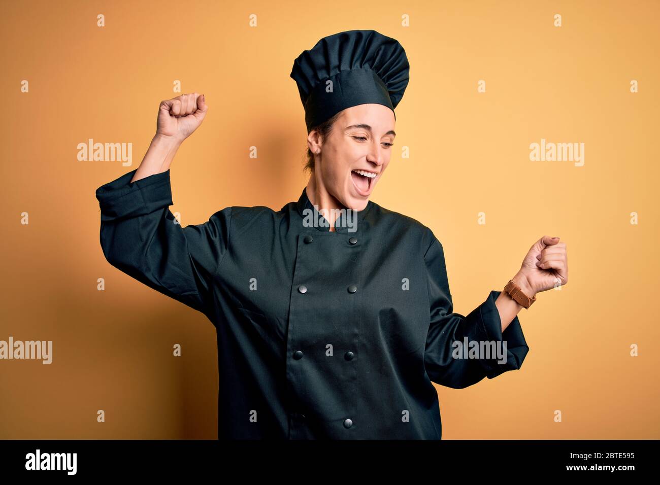 Young beautiful chef woman wearing cooker uniform and hat standing over ...
