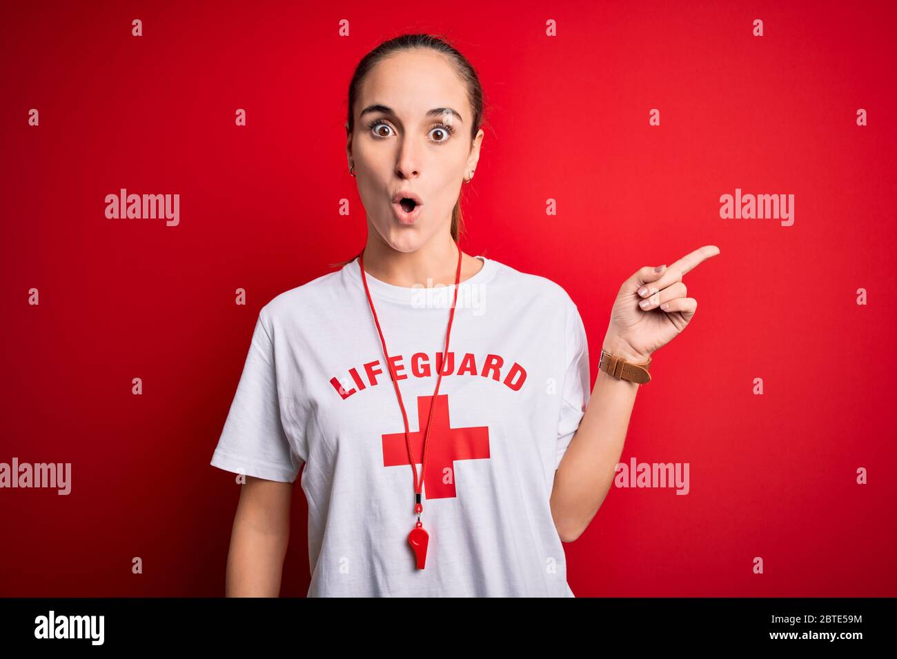Beautiful lifeguard woman wearing t-shirt with red cross using whistle ...
