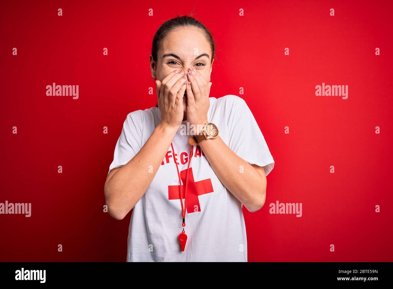 Beautiful lifeguard woman wearing t-shirt with red cross using whistle ...