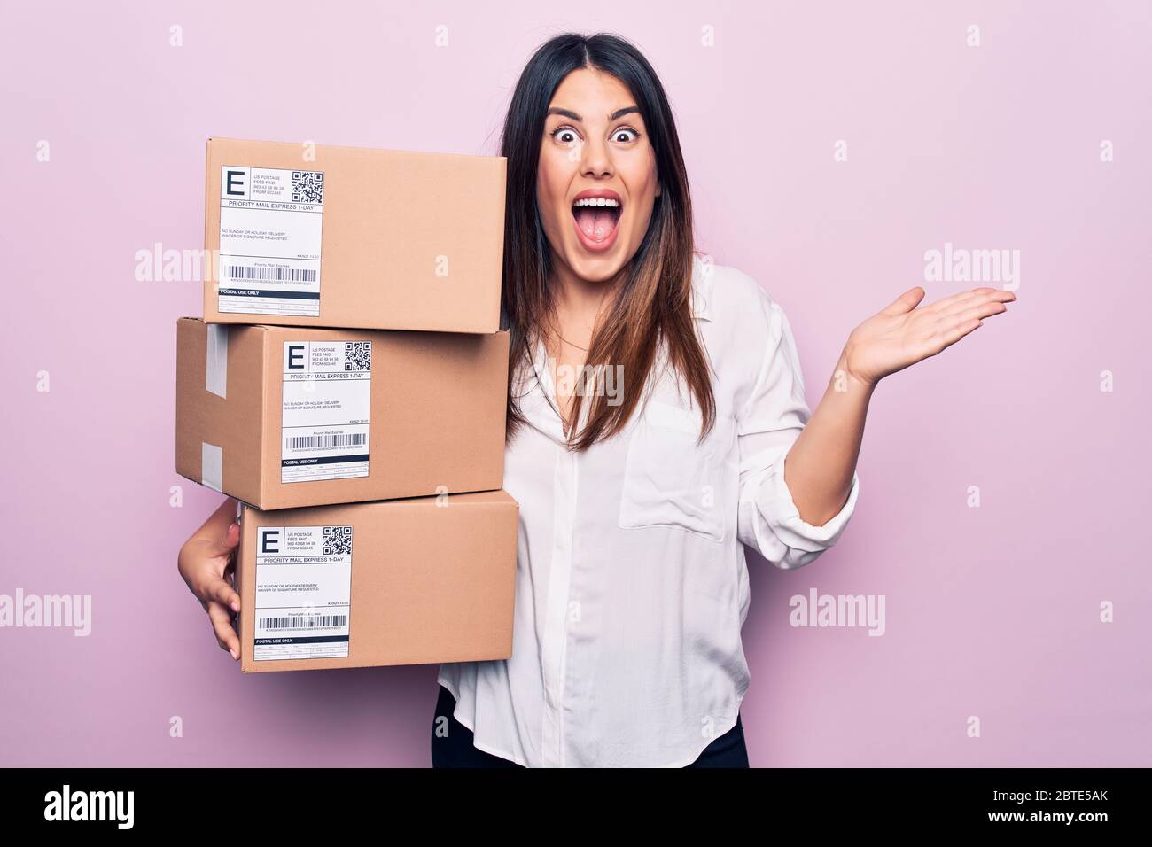 Young beautiful brunette woman holding deliver packages standing over ...