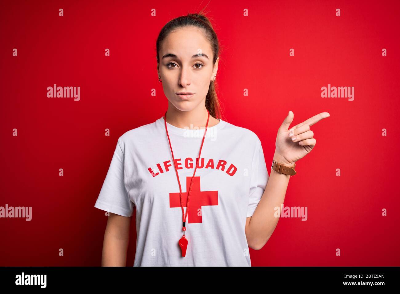 Beautiful lifeguard woman wearing t-shirt with red cross using whistle ...