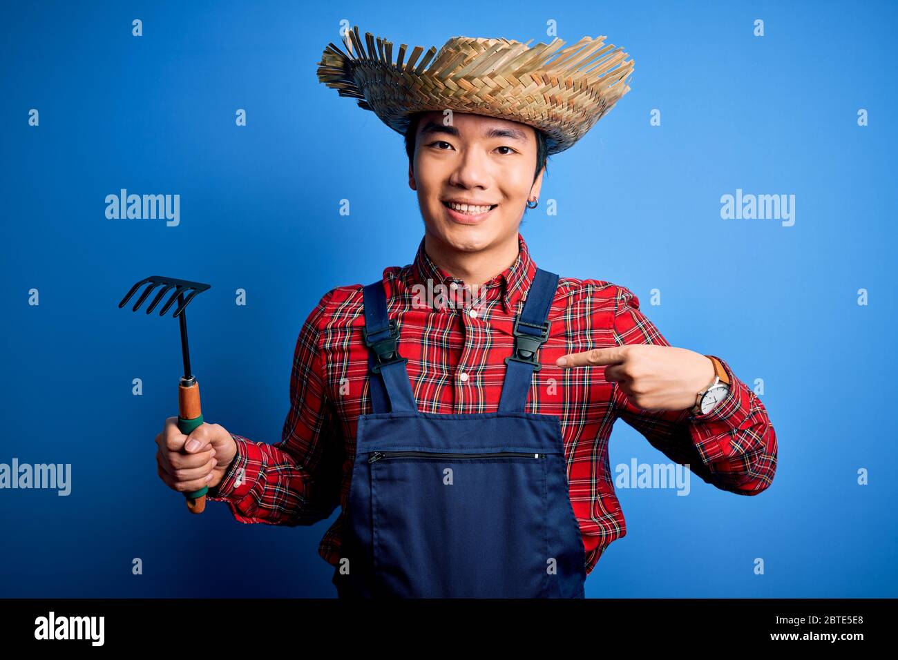 Young handsome chinese farmer man wearing apron and straw hat holding ...