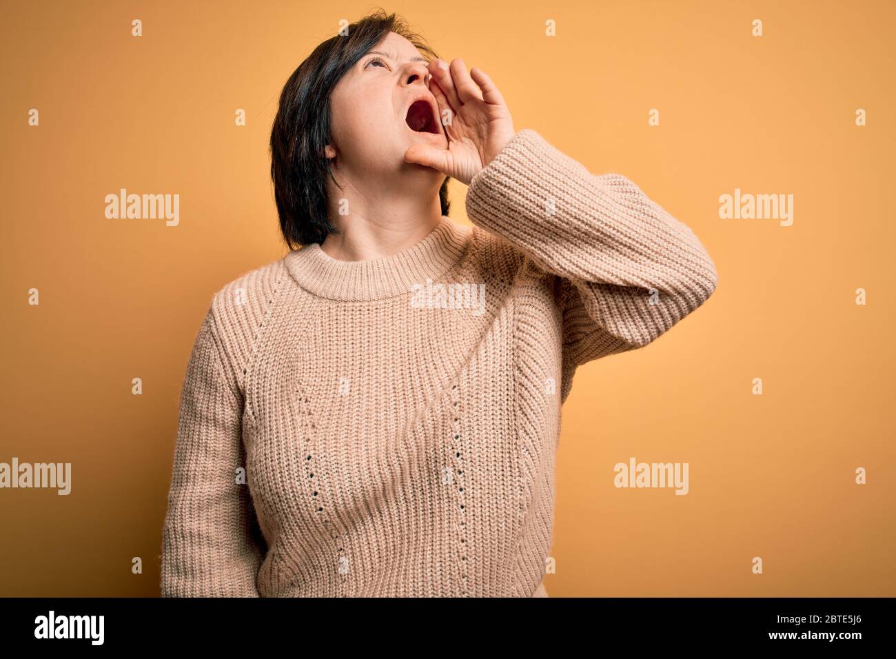 Young down syndrome woman wearing casual sweater over yellow background ...
