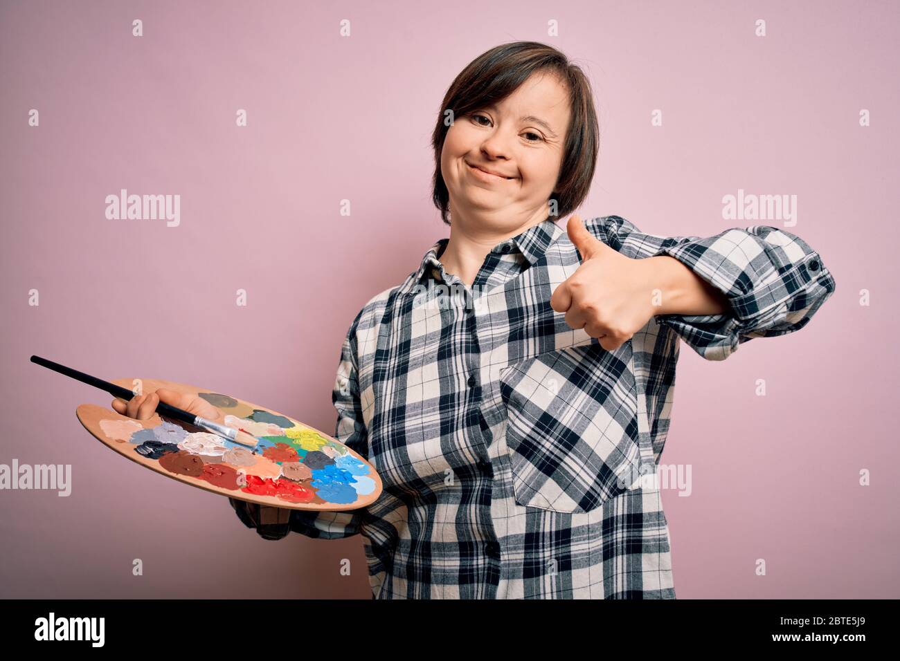 Young down syndrome artist woman holding painter palette and paintbrush ...