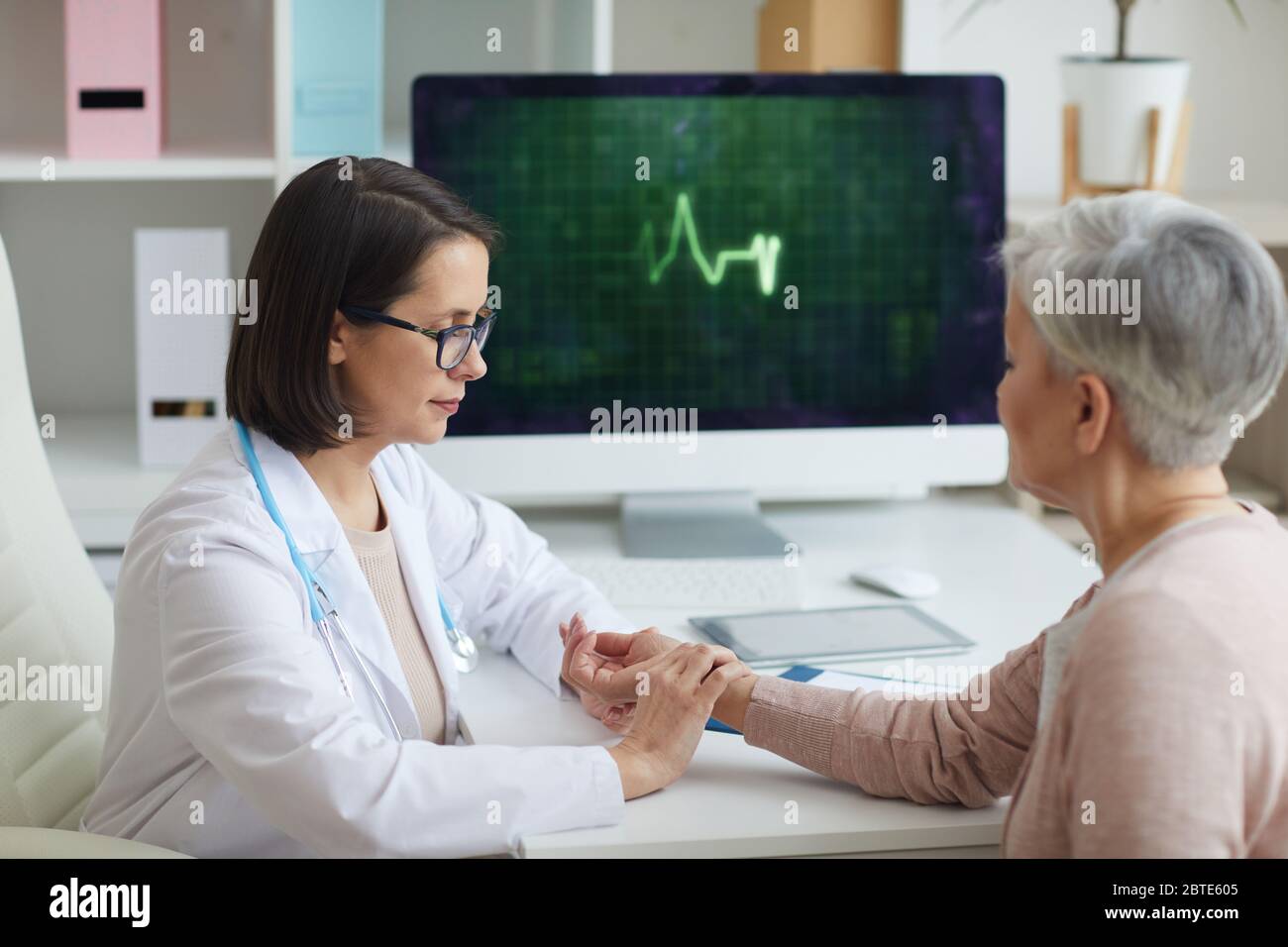 Side View Portrait Of Female Doctor Checking Heart Rate Of Senior