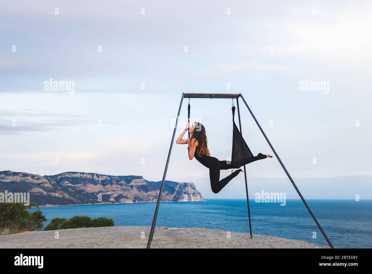 Woman practice acrobatic fly dance yoga outdoors with sea and mountain ...