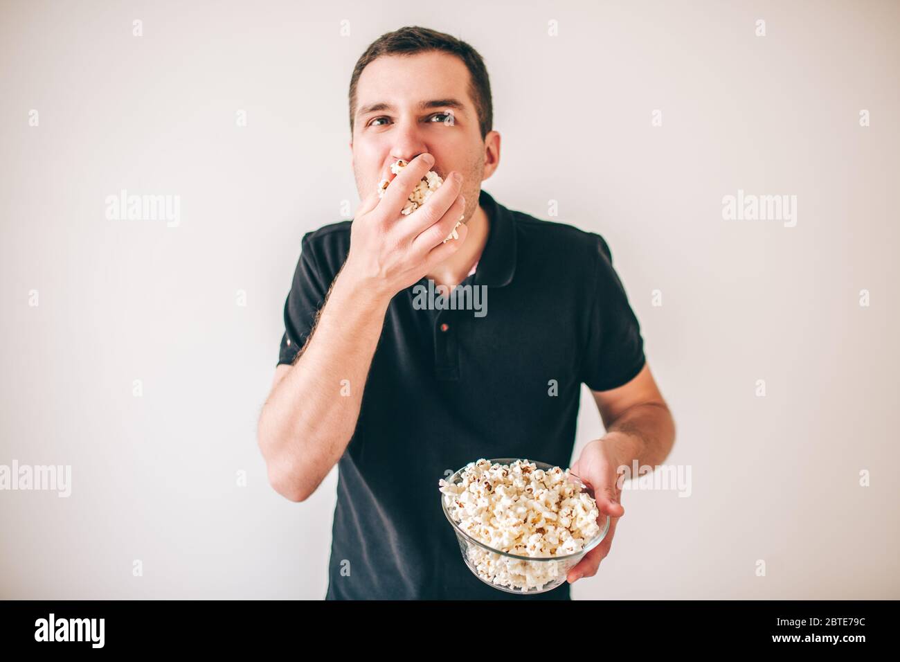 Young man isolated over white background. Guy eating popcorn from bowl ...