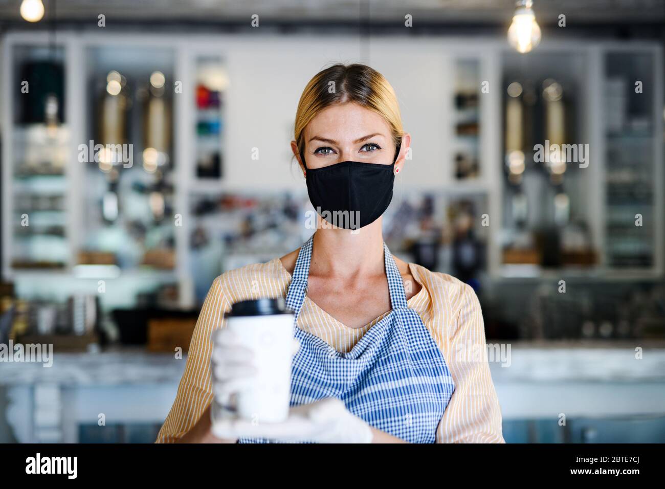Woman owner with face mask in coffee shop, lockdown and back to normal ...
