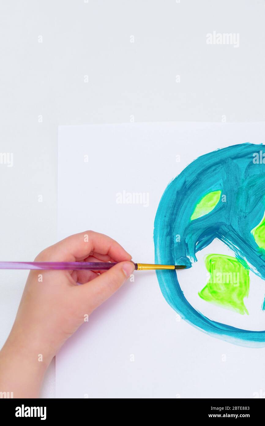 Close up of child's hand drawing planet Earth with a brush by acrylic ...