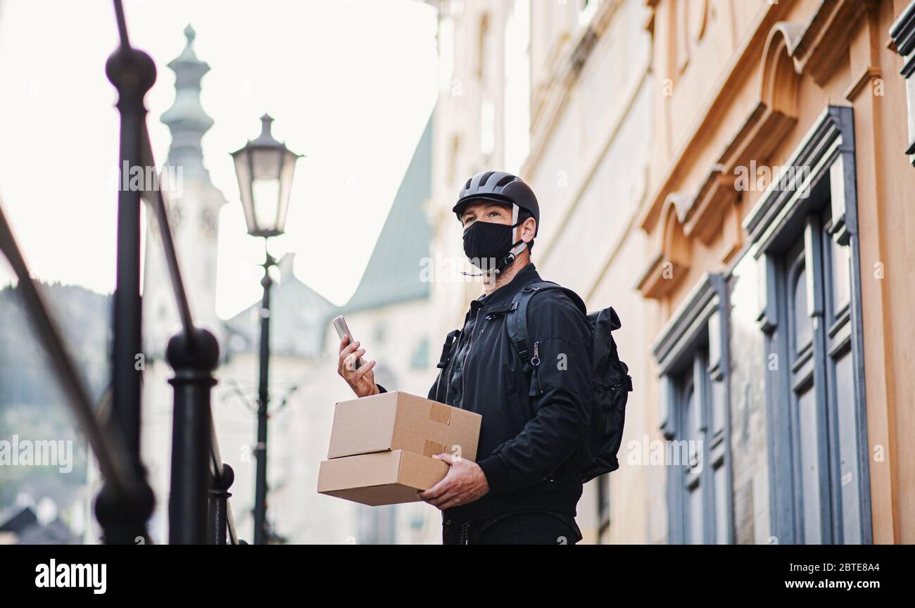 Delivery man courier with face mask and smartphone delivering in town ...
