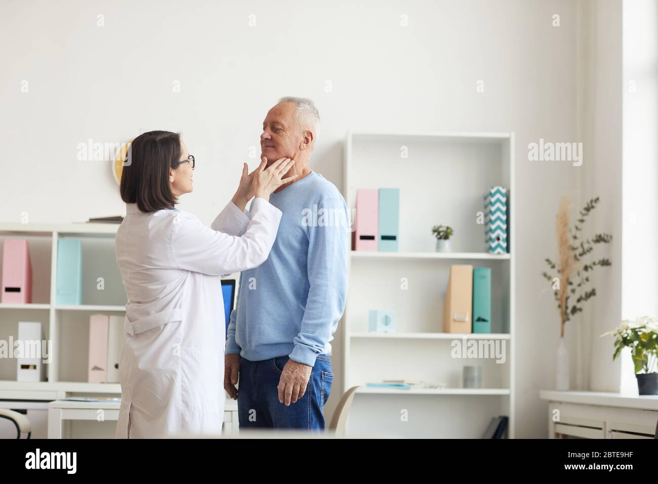 Wide angle portrait of female doctor palpating neck of senior patient ...