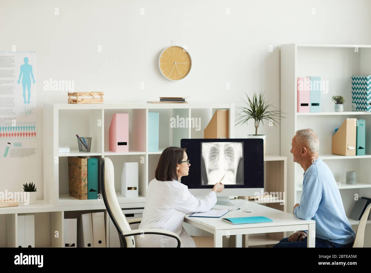 Wide angle side view at female doctor pointing at x-ray image of lungs ...
