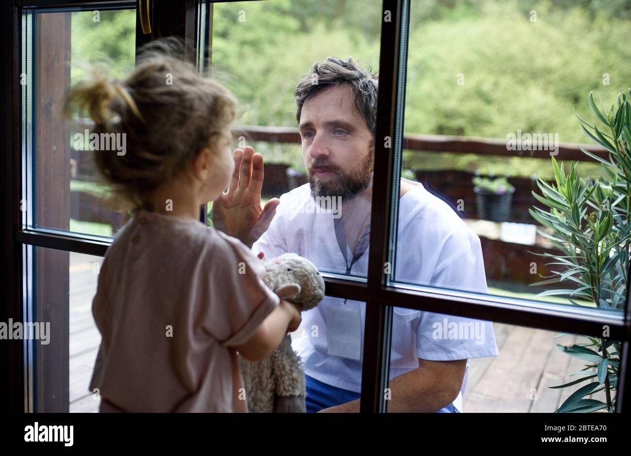 Doctor coming to see family in isolation, window glass separating them ...