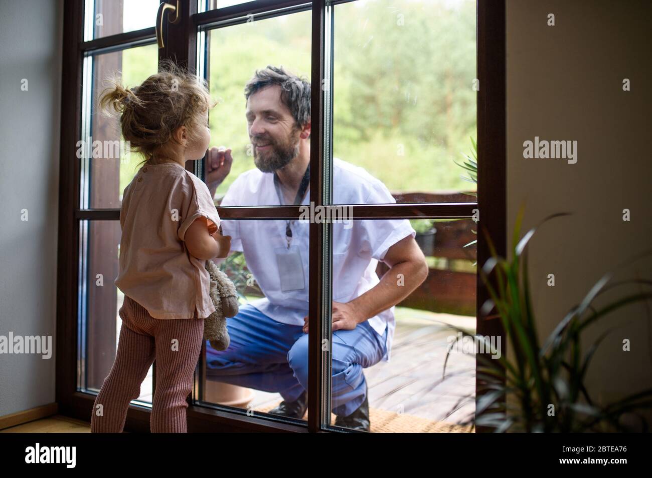 Doctor coming to see family in isolation, window glass separating them ...