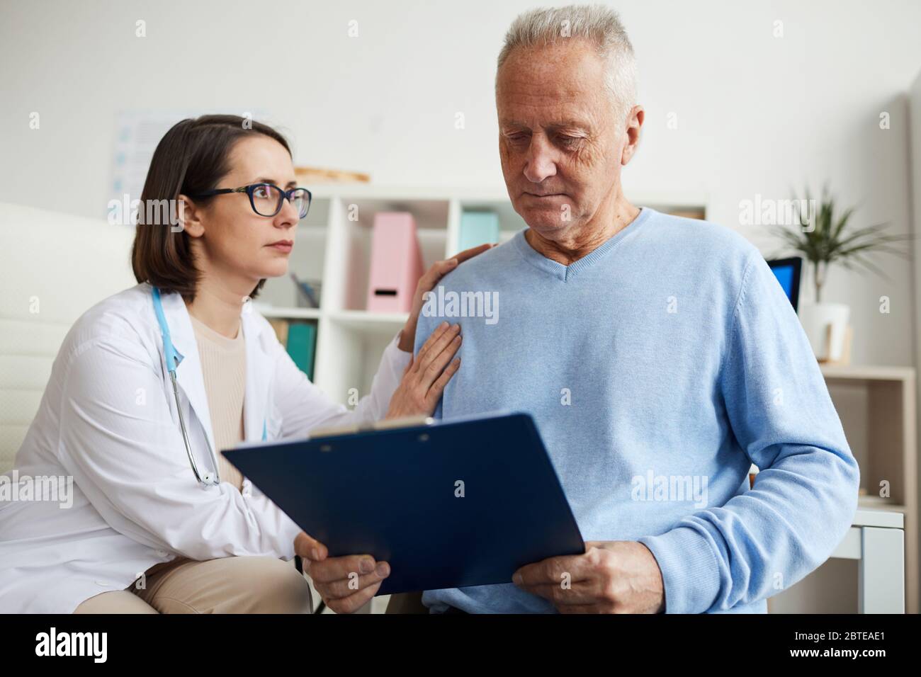 Portrait of caring female doctor comforting senior patient reading ...