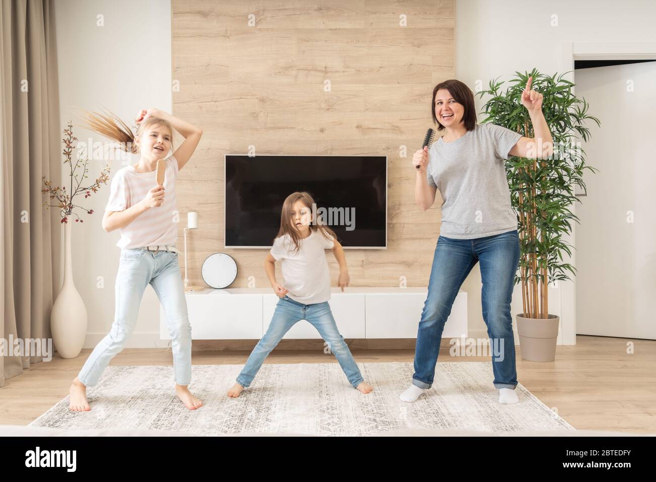 Happy mother and two daughters having fun singing karaoke song in hairbrushes. mother laughing ...