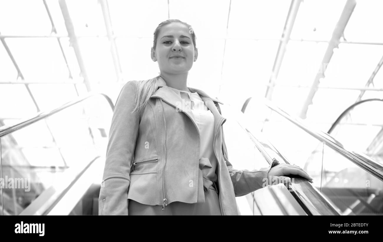 Black and white portrait of beautiful young woman standing on escalator ...
