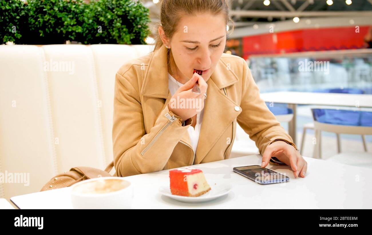 Portrait of beautiful young woman eating dessert and reading news on ...