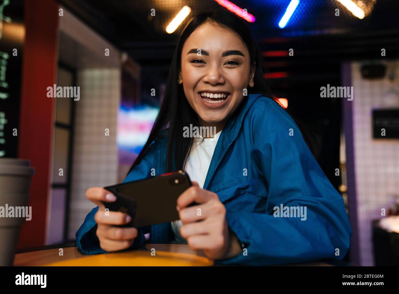 Photo of laughing asian woman playing video game on mobile phone while ...
