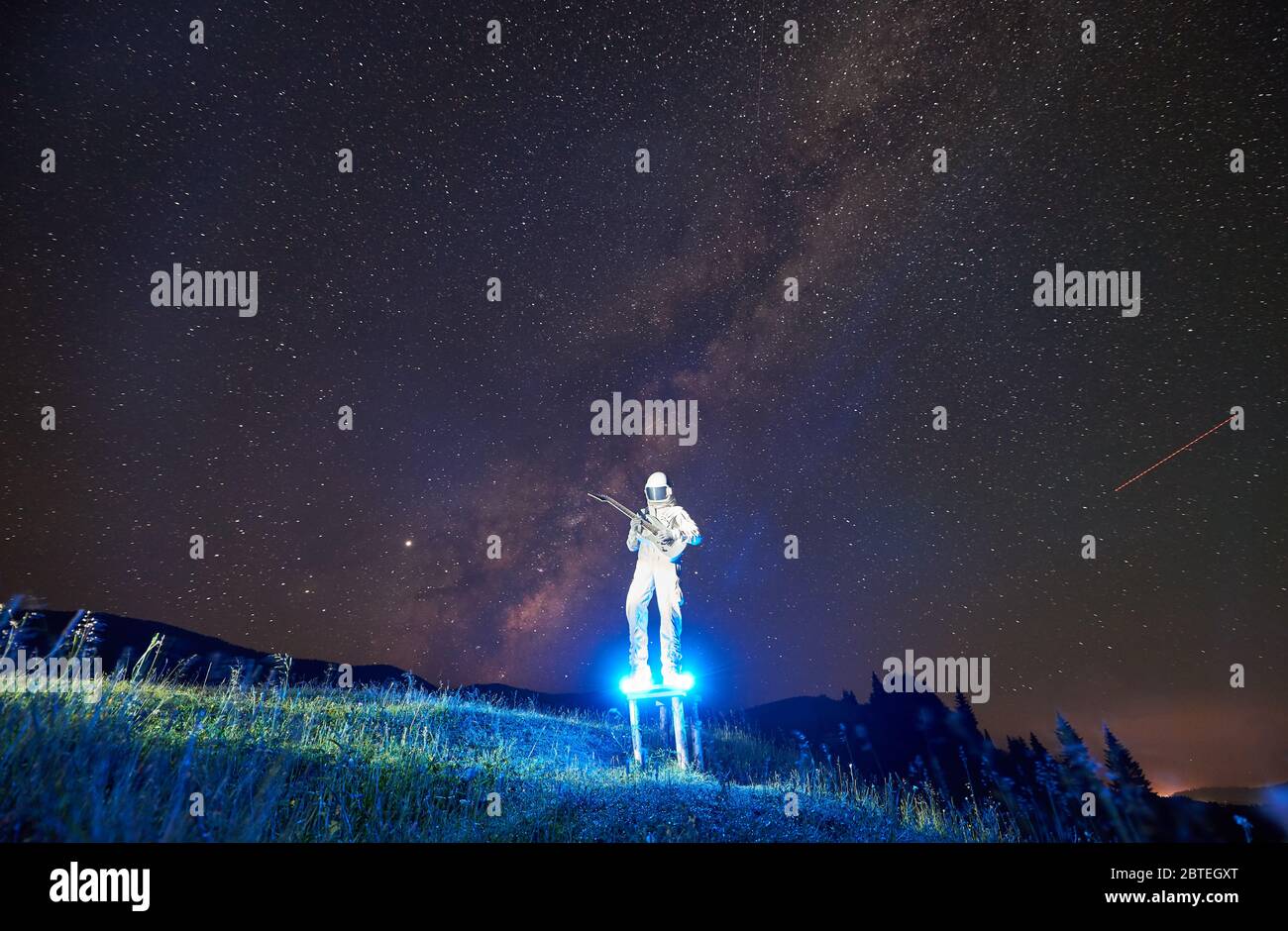 Astronaut with glowing boots playing guitar under starry sky with Milky ...