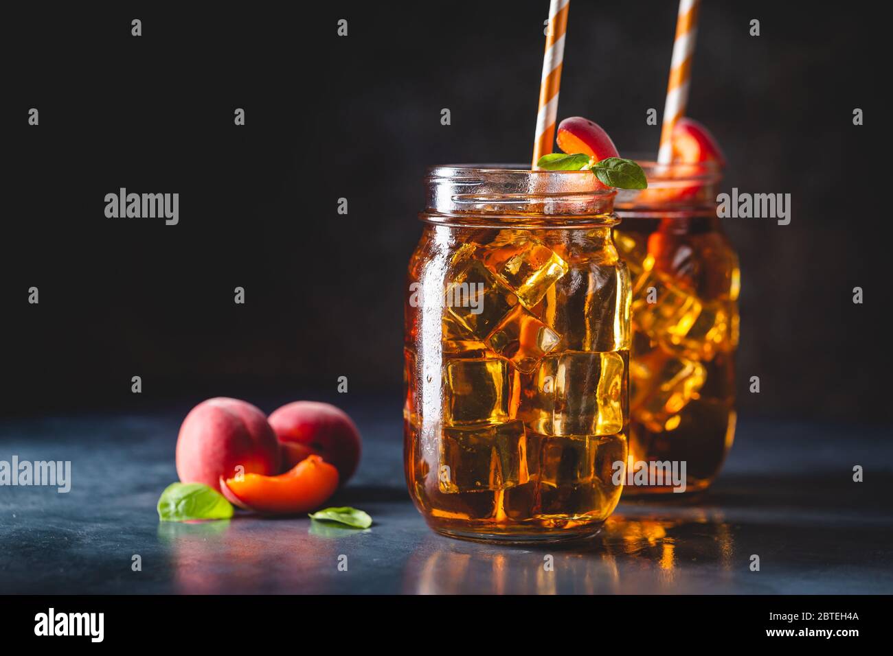 Glass of peach or apricot iced tea with fruit slices against dark blue ...