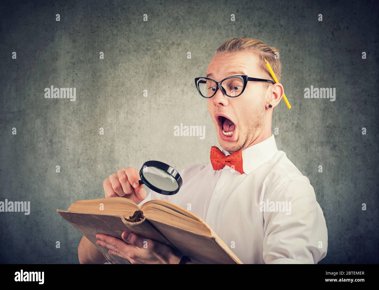 Shocked young man with magnifying glass reading an ancient book feeling ...