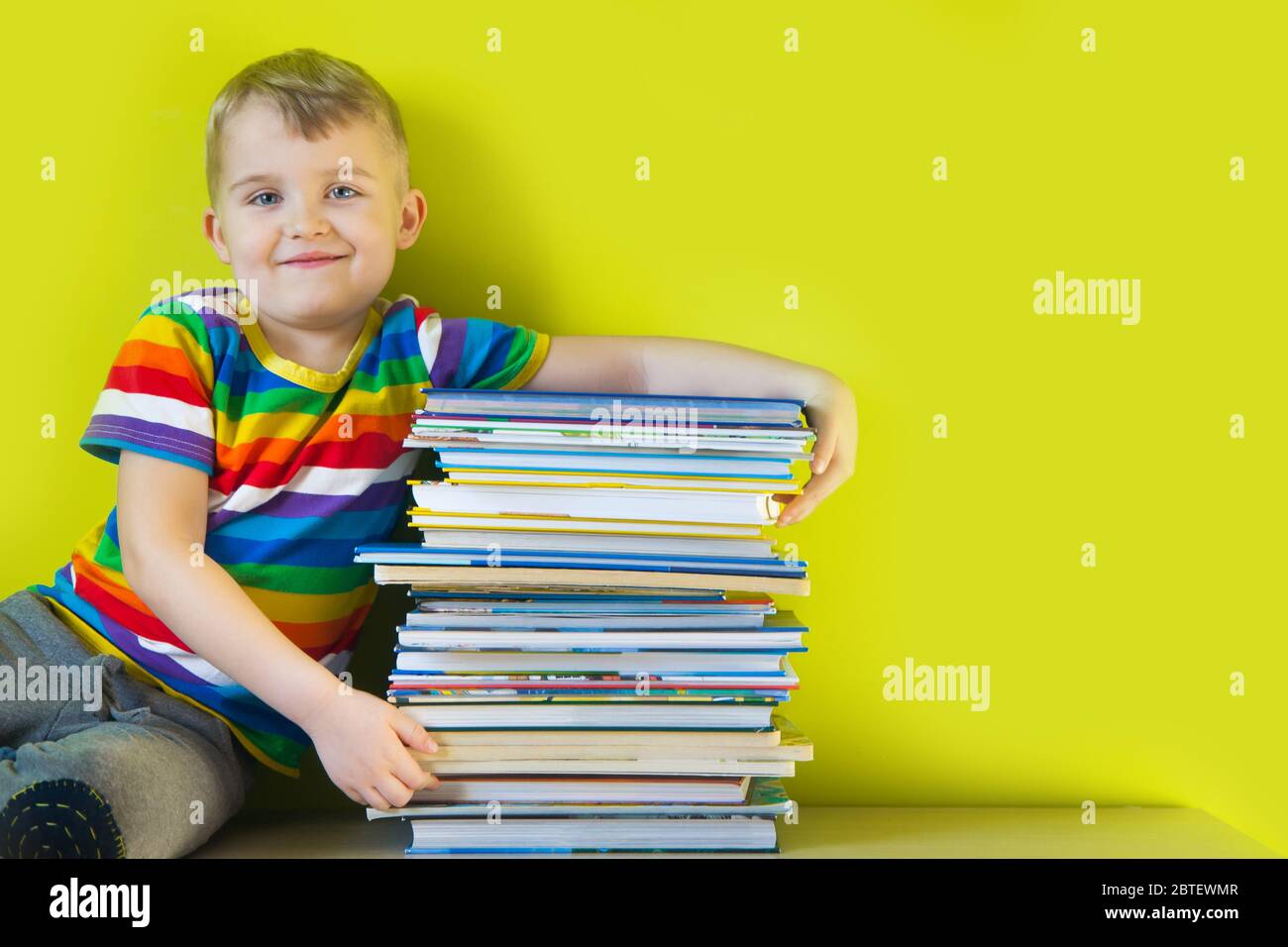 The child holds a large stacked of children's books in his hands. Green ...
