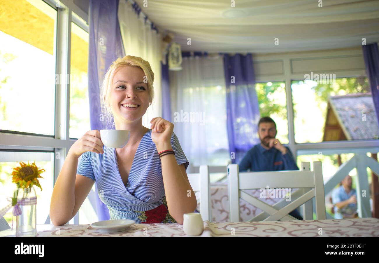 Cafe and service concept. Girl drinks coffee or tea in cafe or ...