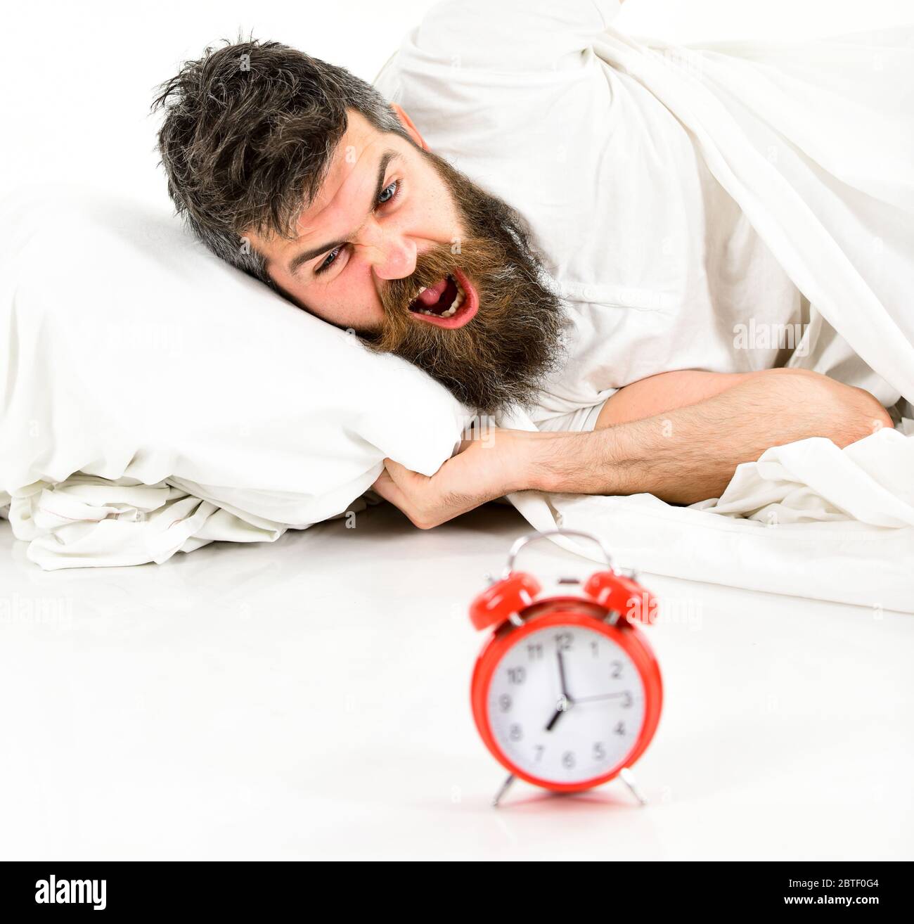 Guy with furious shouting face looks at alarm clock. Man suffers in ...
