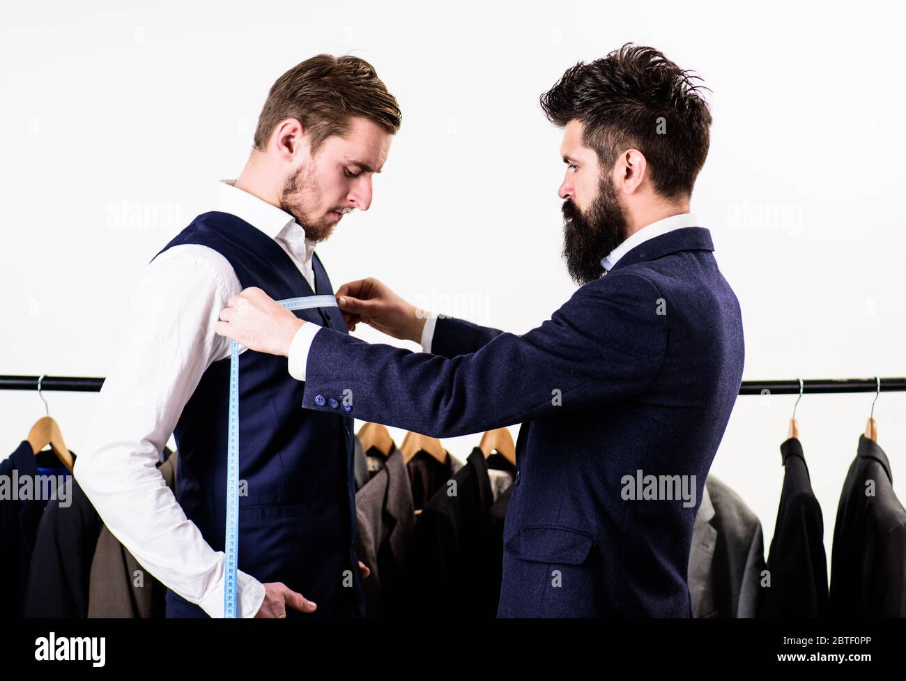 Businessman, client stand near hanger with suits while tailor working ...